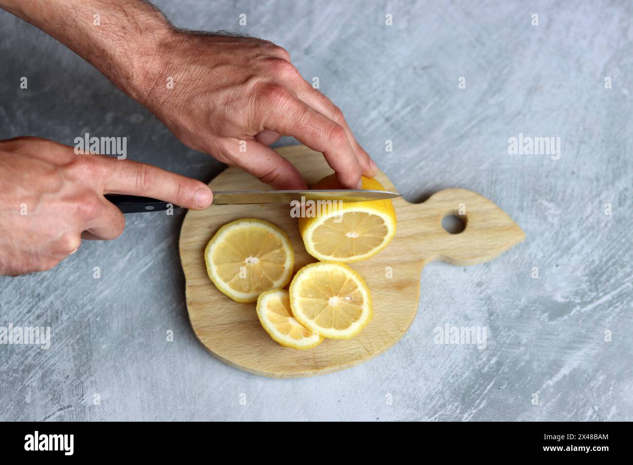 Male hands cutting lemon on wooden board. Grey background with copy ...