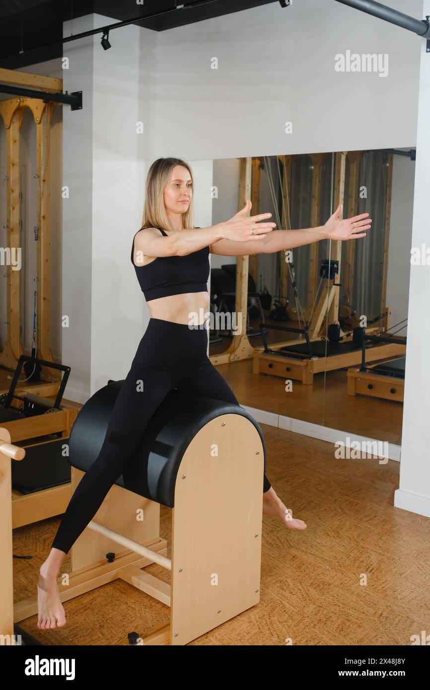Young girl doing Pilates barre in a gym. Beautiful slim woman in black ...