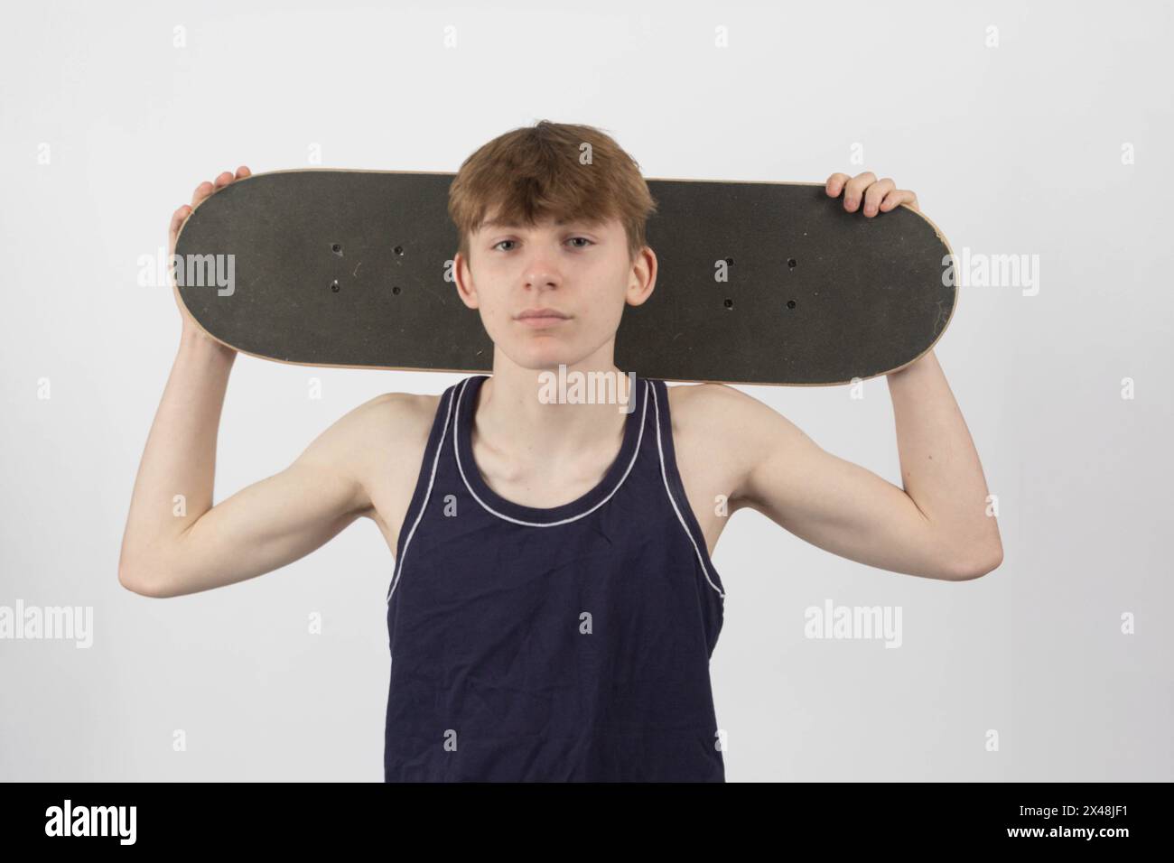 A fifteen year old skater boy holding a skateboard behing his head ...