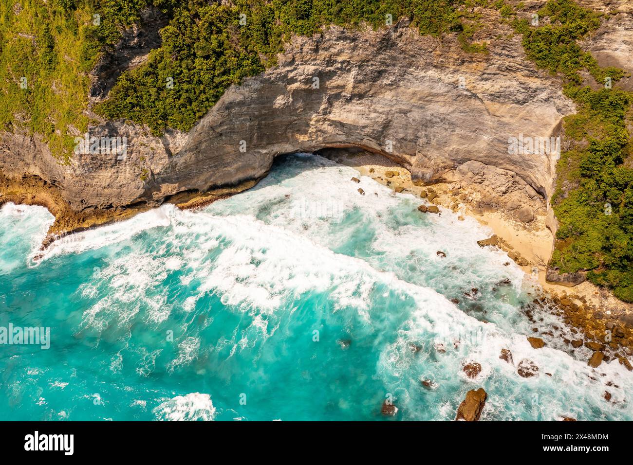 Ocean waves crash against rocks covered with greenery, forming white ...