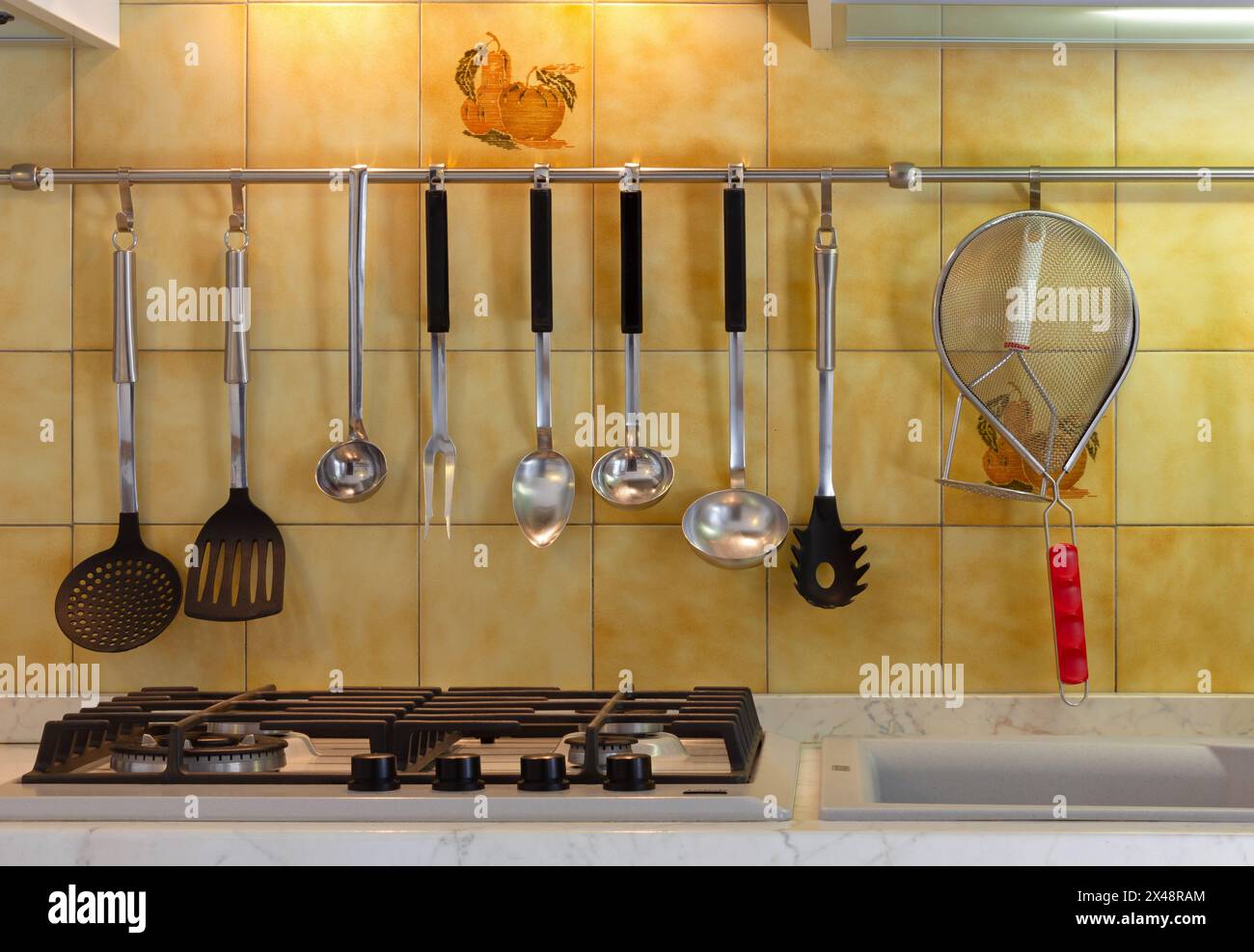 Stove of a modern kitchen with utensils hanging from a metal bar Stock ...