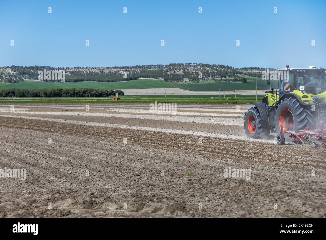 A farmer with her tractor carrying a plow raking large fields of crops ...