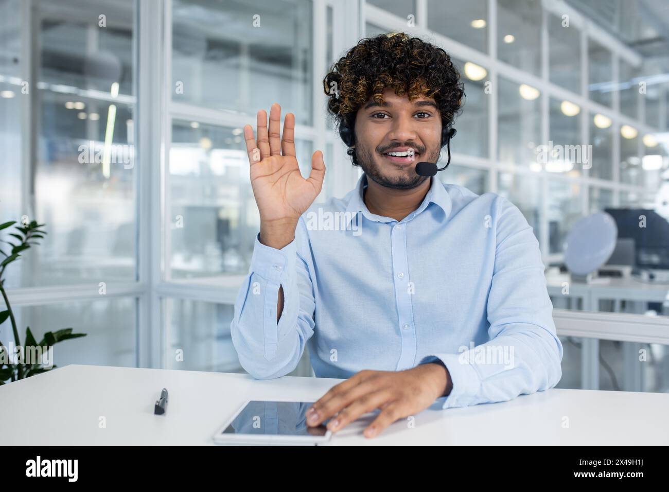 Hindu male wearing headset with microphone and raising hand in greeting ...