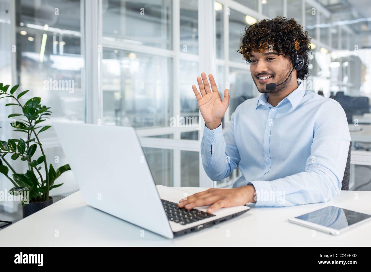 Sincere hispanic person in headset with microphone waving hello and ...