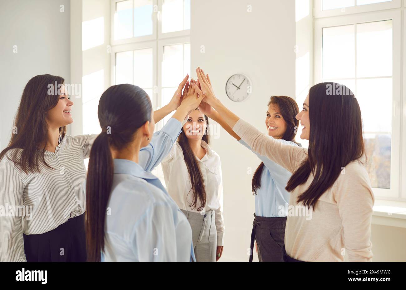 Smiling happy business people women putting their arms together in a ...