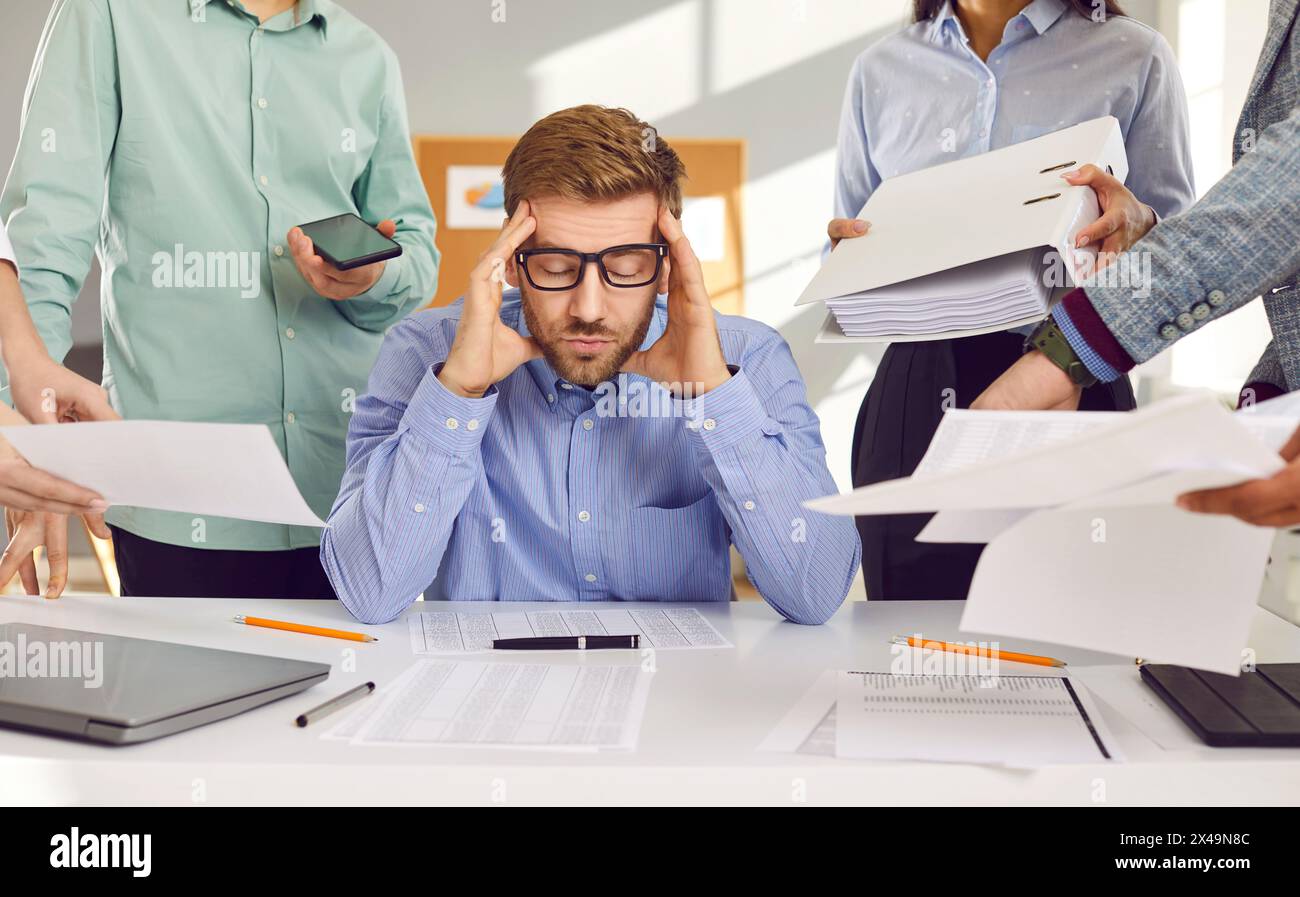 Stressed, tired man sitting at office desk and ignoring workers giving ...