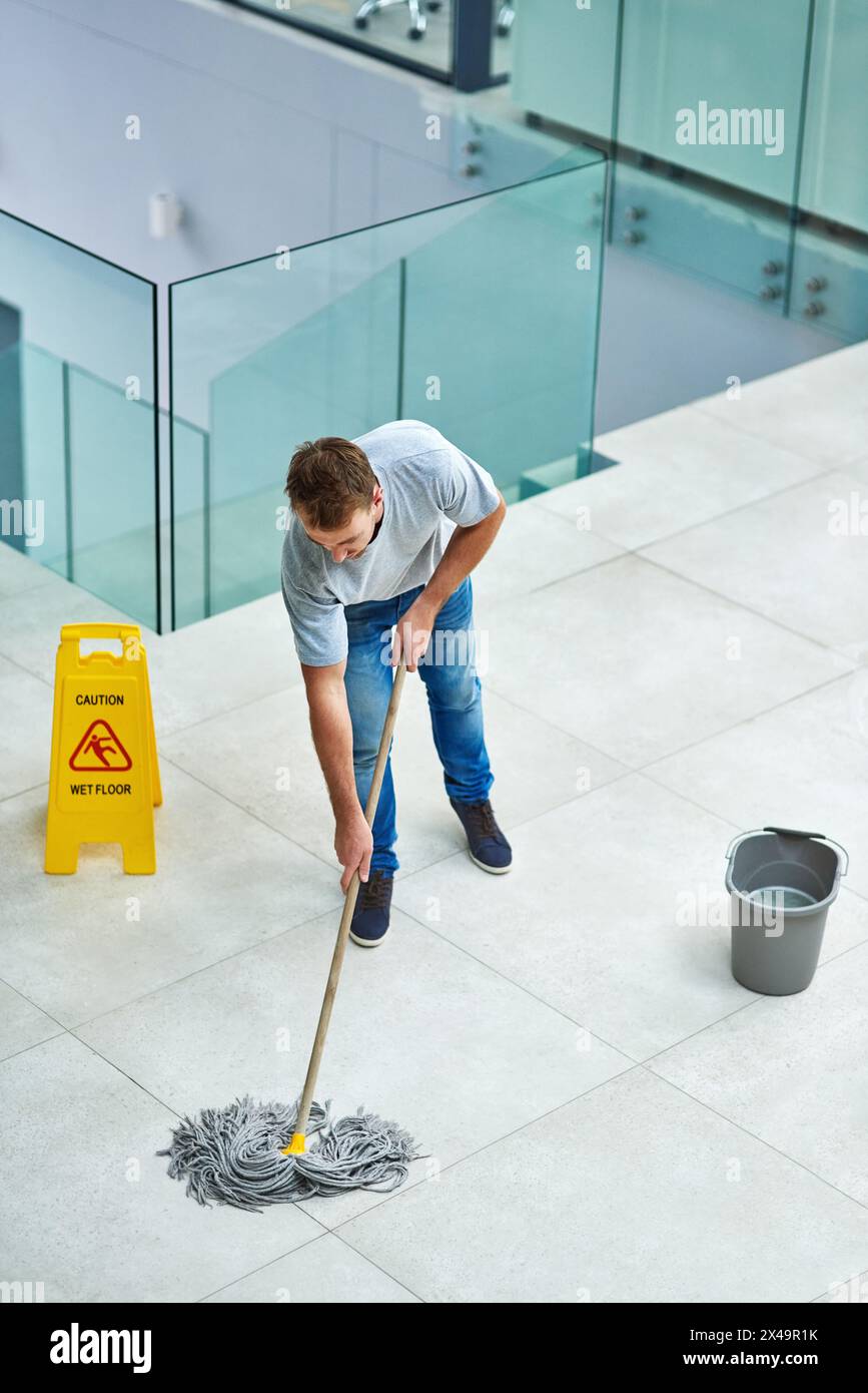 Man, janitor and mopping office floor or cleaning hygiene with caution ...