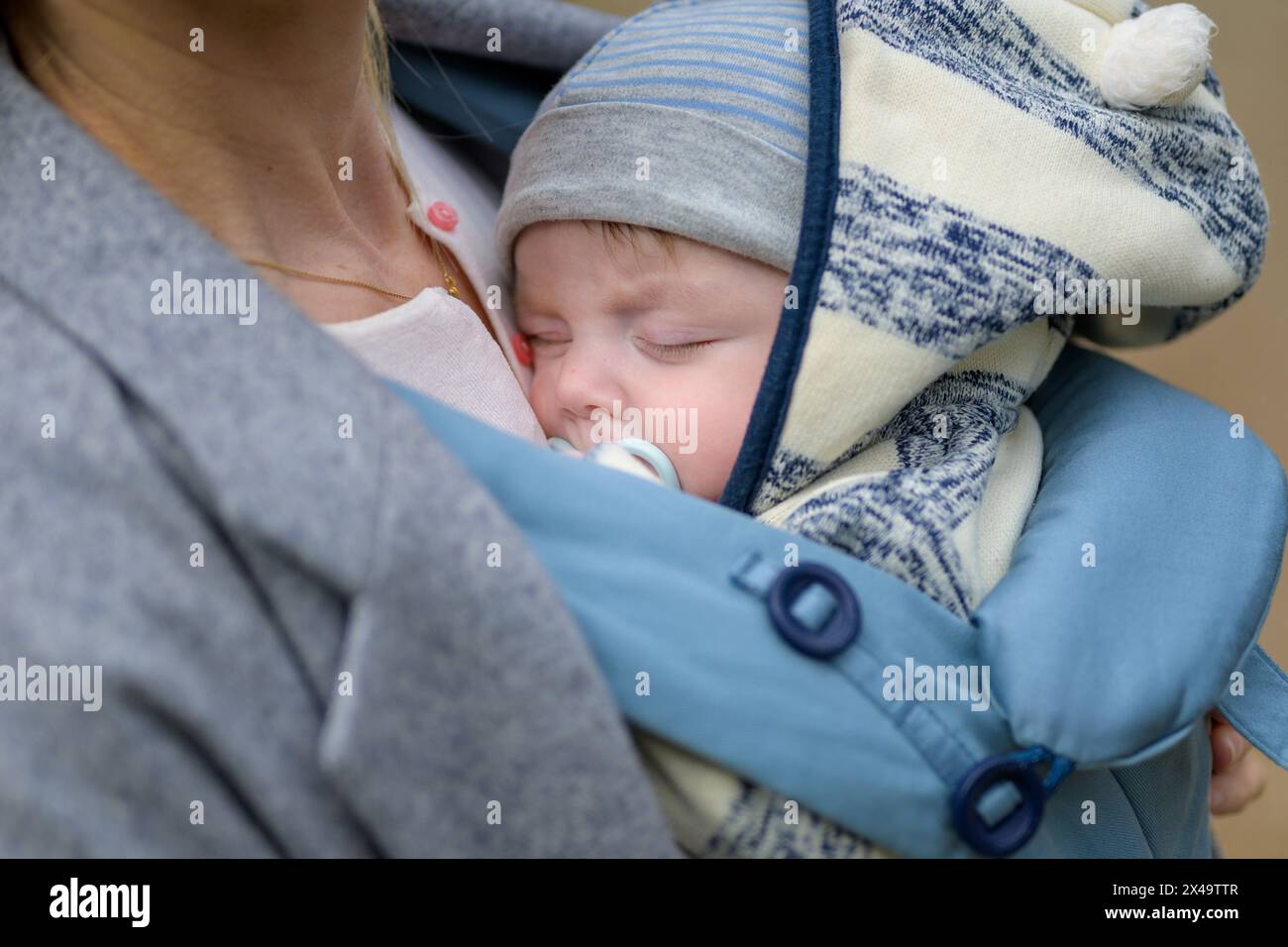 Close up of a baby sleeping in a baby carrier on his mother's chest or ...