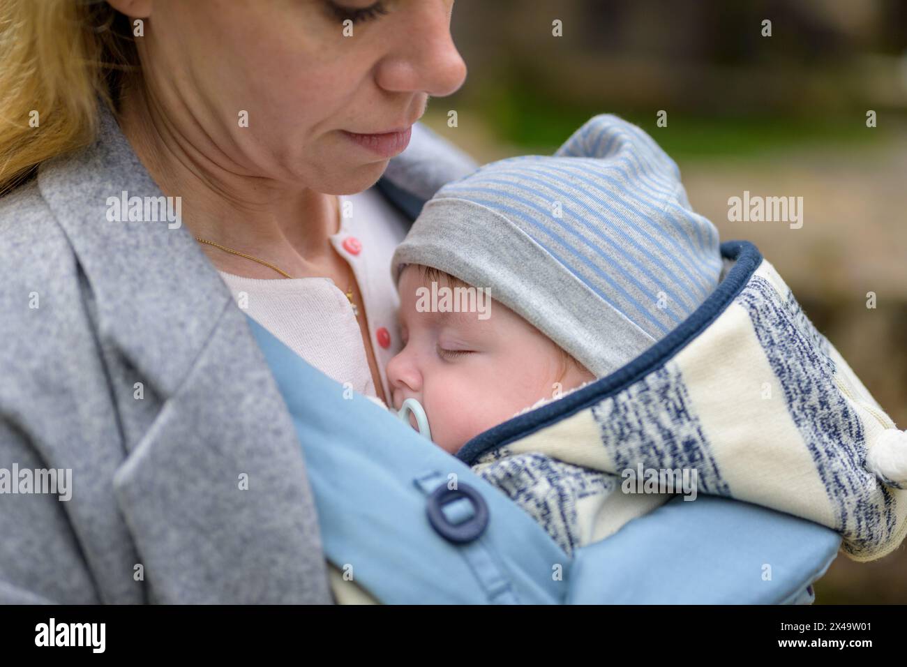 Close up of a baby sleeping in a baby carrier on his mother's chest or ...