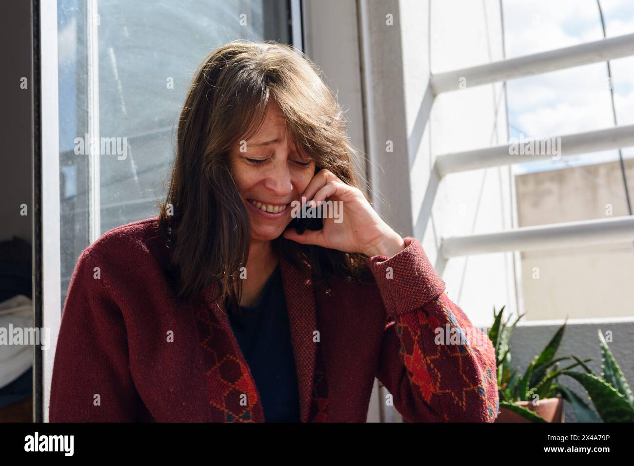 Latin adult woman sitting on balcony of her house crying sad talking on ...