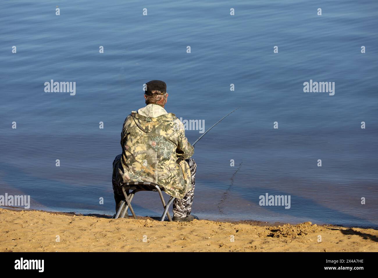Fisherman sitting near the water with a fishing rod, rear view. Man ...