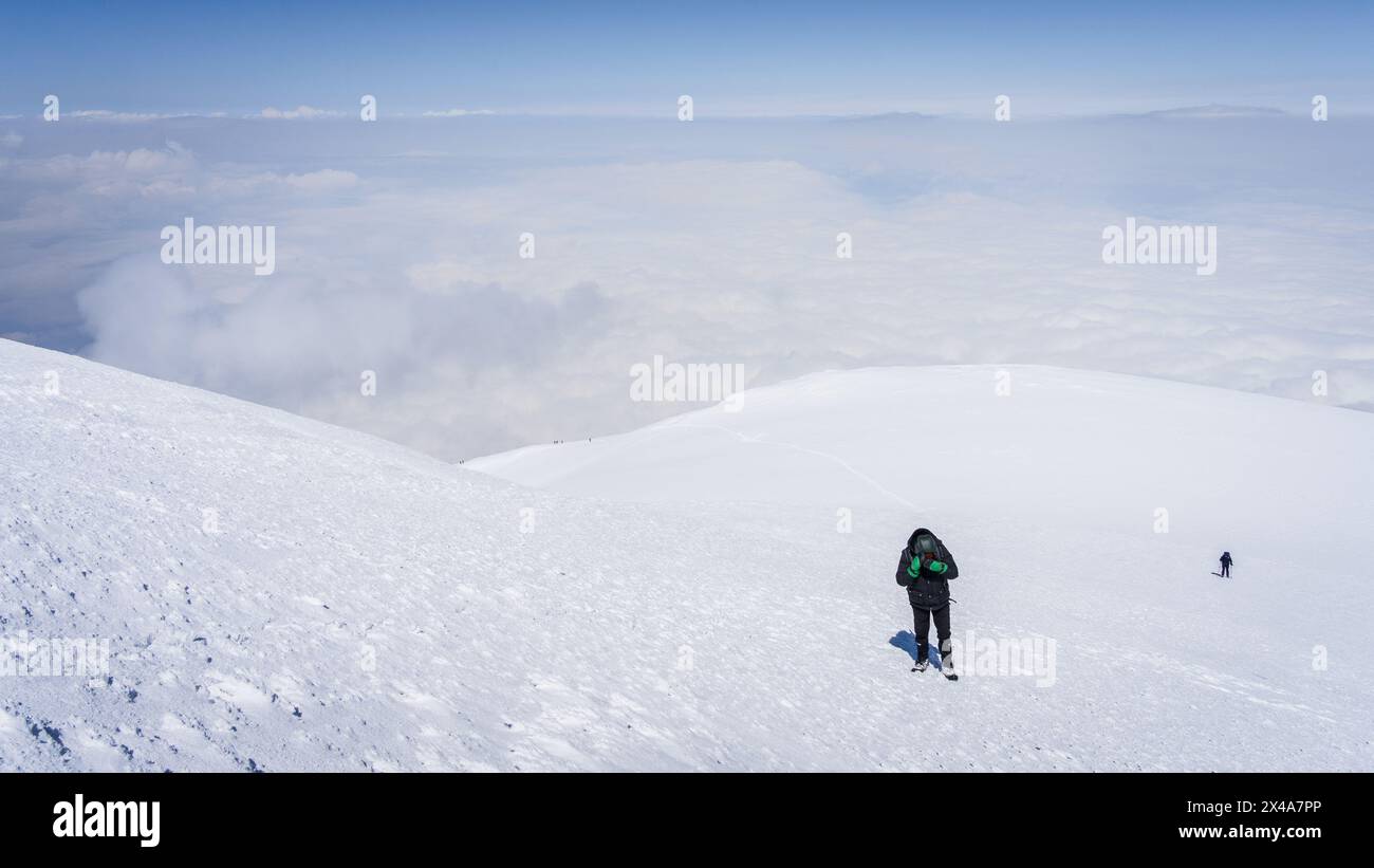 Mountaineers walking towards the snowy mountain summit above the clouds ...