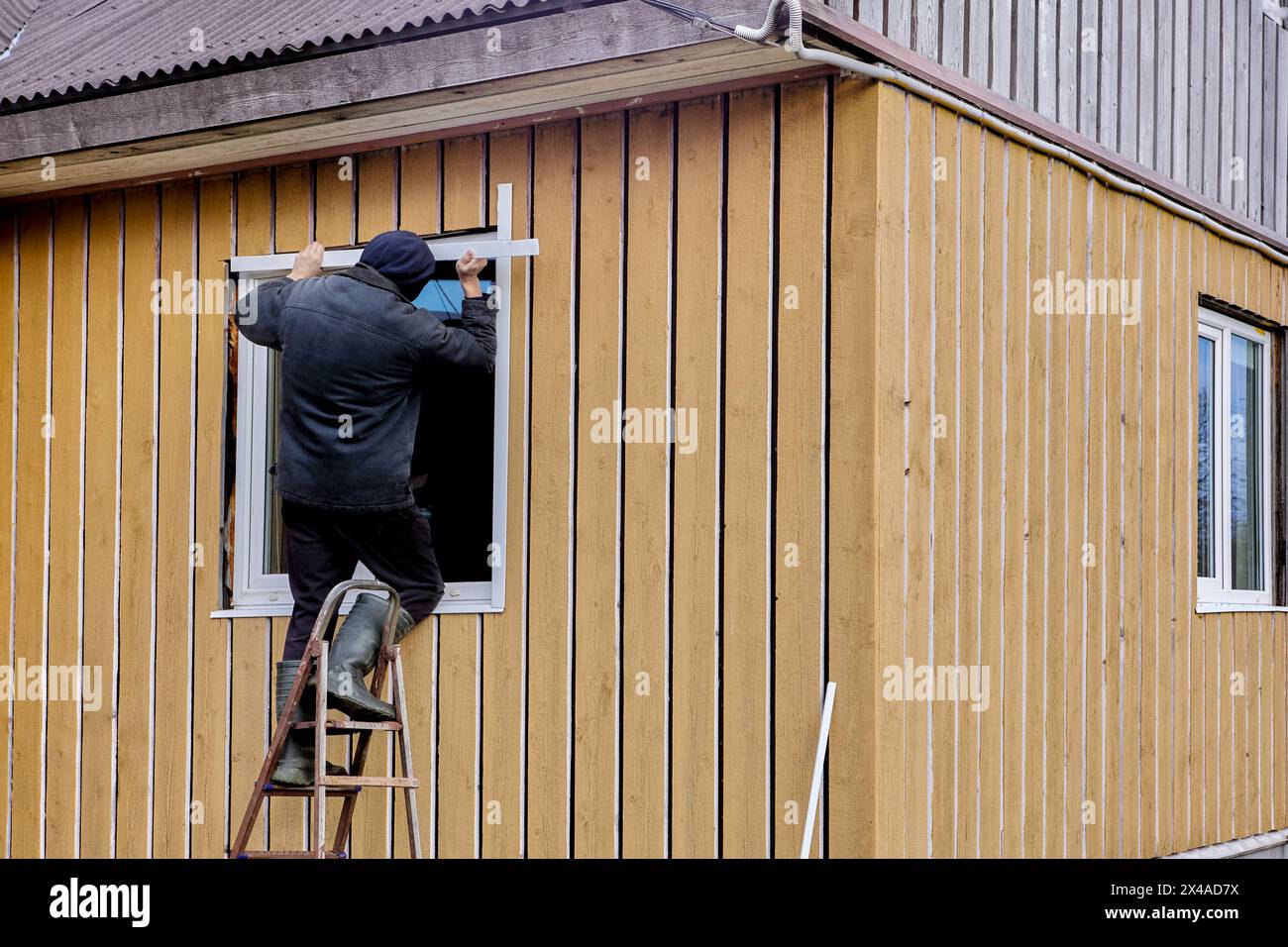 Construction worker uses stepladder to install metal jambs on window on ...