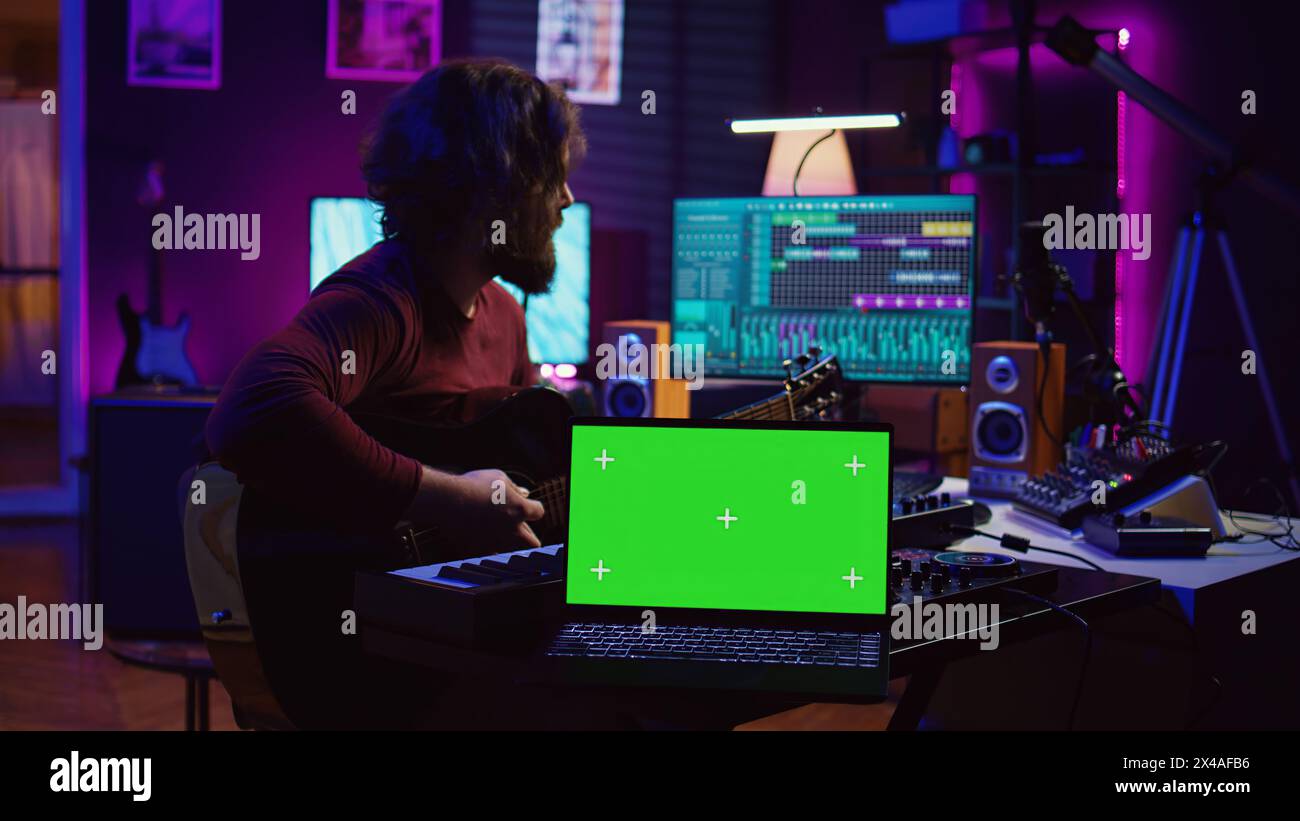 Guitarist playing his acoustic instrument next to greenscreen on laptop ...