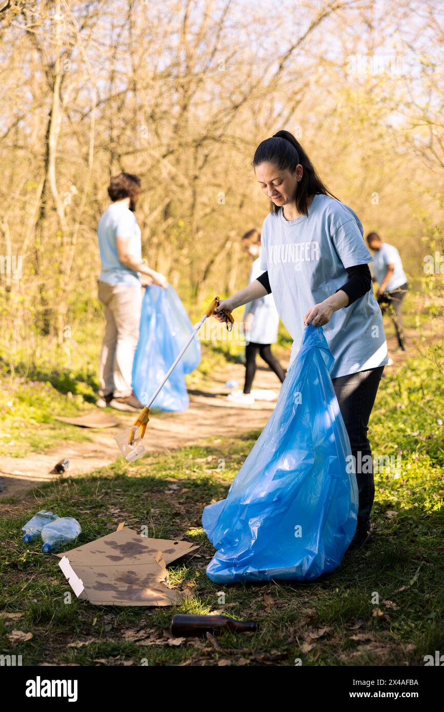 Female volunteer tidying the woodland of garbage and plastic bottles ...
