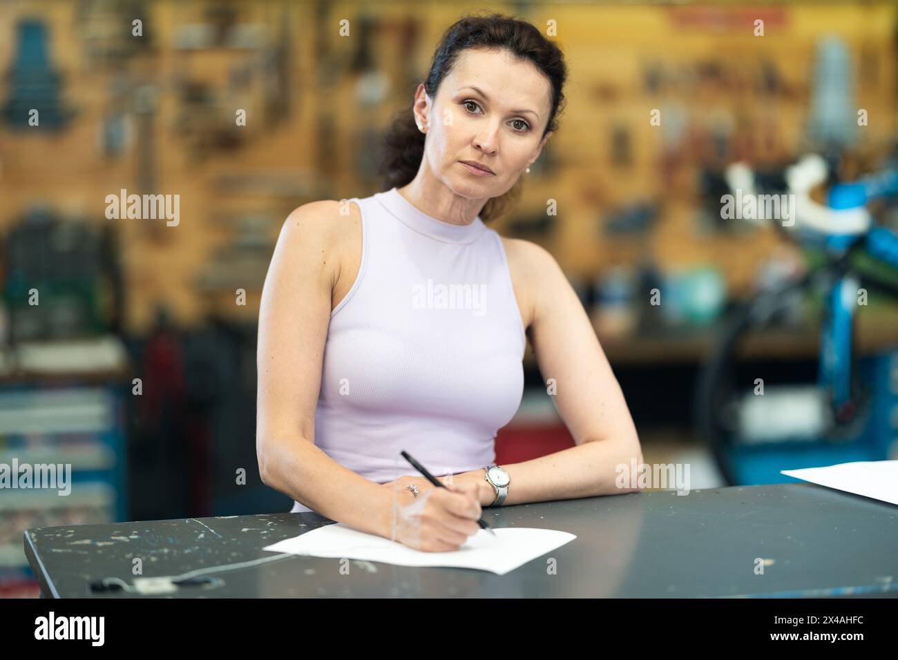 Portrait of young woman seller posing behind counter and writing order ...