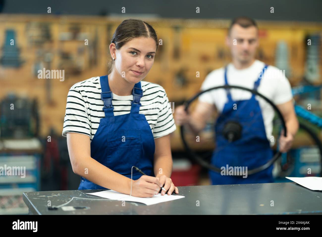 Polite young girl salesperson dressed in uniform taking order and writing form in sports store ...