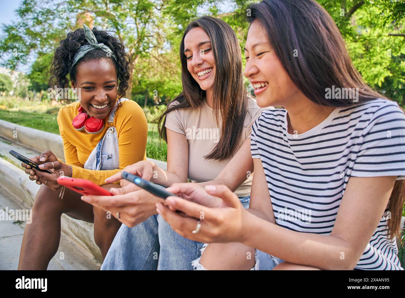 three young women are sitting on a bench looking at their cell phones ...