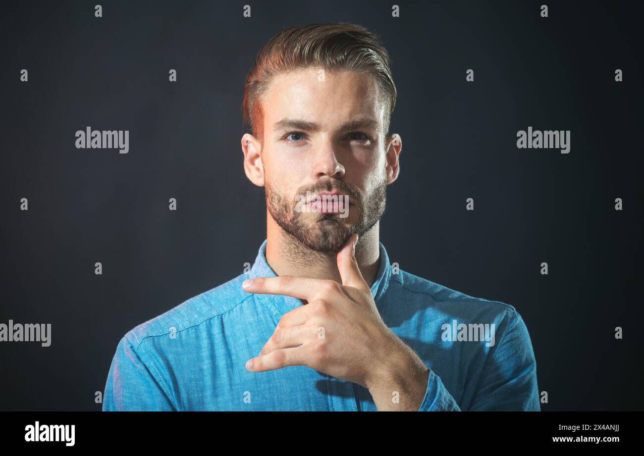 Pensive thoughtful unshaven man in denim shirt with hand on chin making ...
