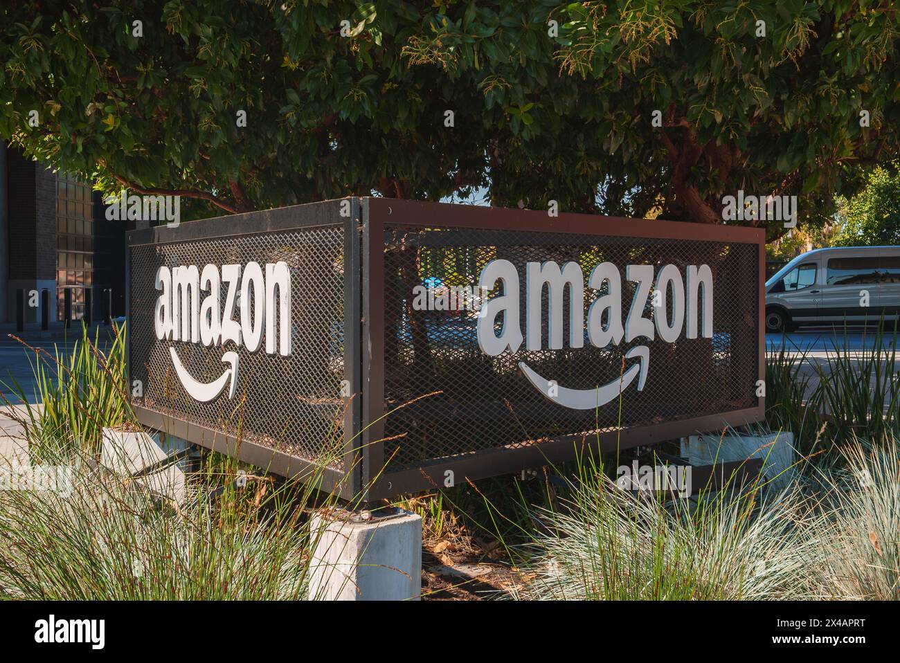 Large metal Amazon logo sign outdoors near road with green landscaping ...