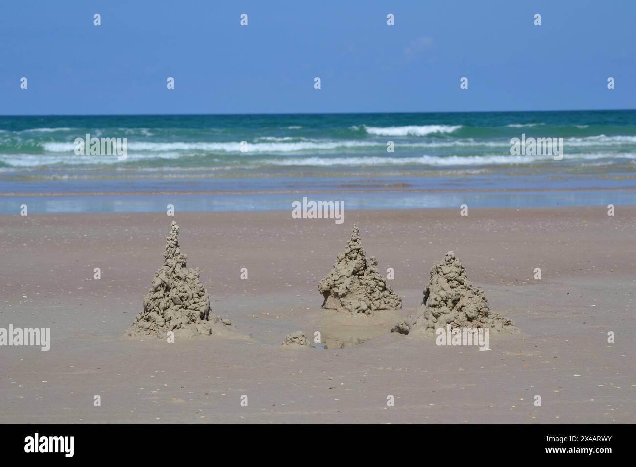 Three drip sandcastles stand on the sandy beach, with the stunning aqua ...
