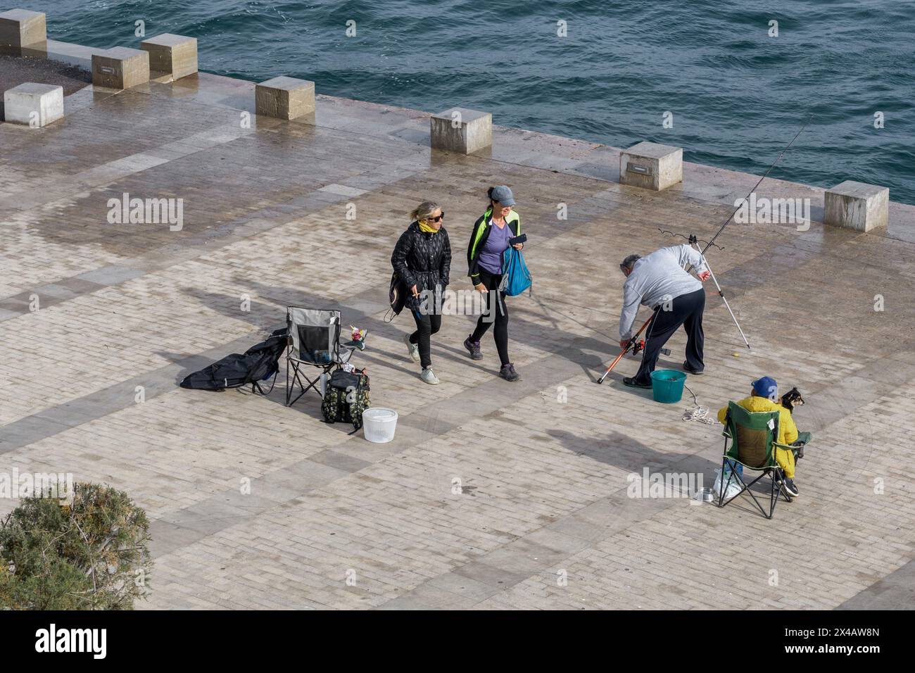 two women walking, one sitting and a man placing the fishing rod in the ...