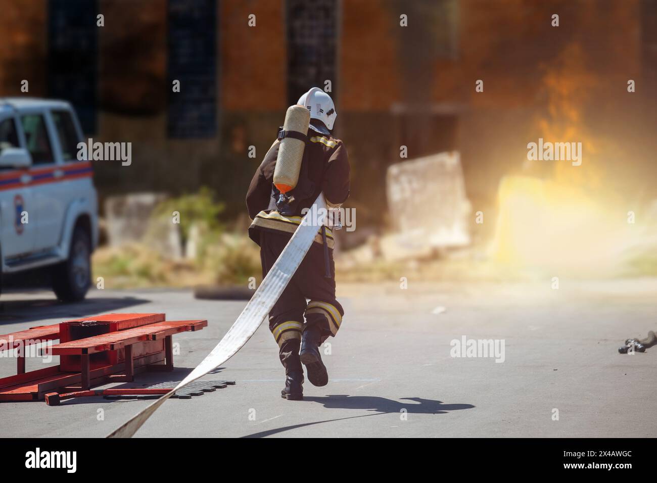 Firefighter with hose running to burning industrial building Stock ...