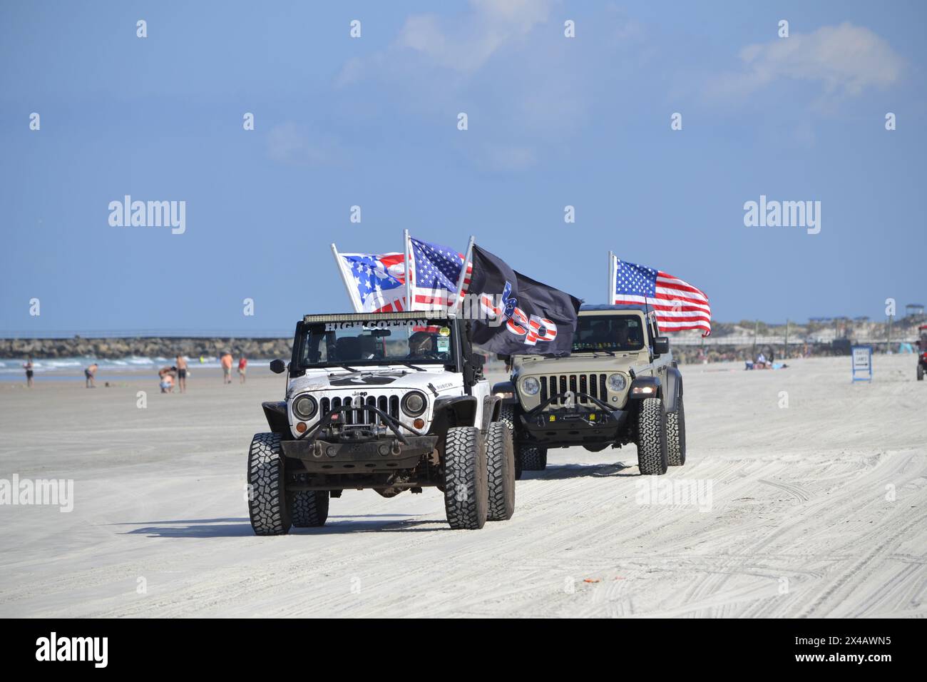 Two Jeeps traverse the sandy beach, American flags waving, against the ...