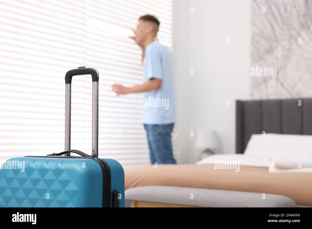 Guest looking through blinds in stylish hotel room, focus on suitcase ...