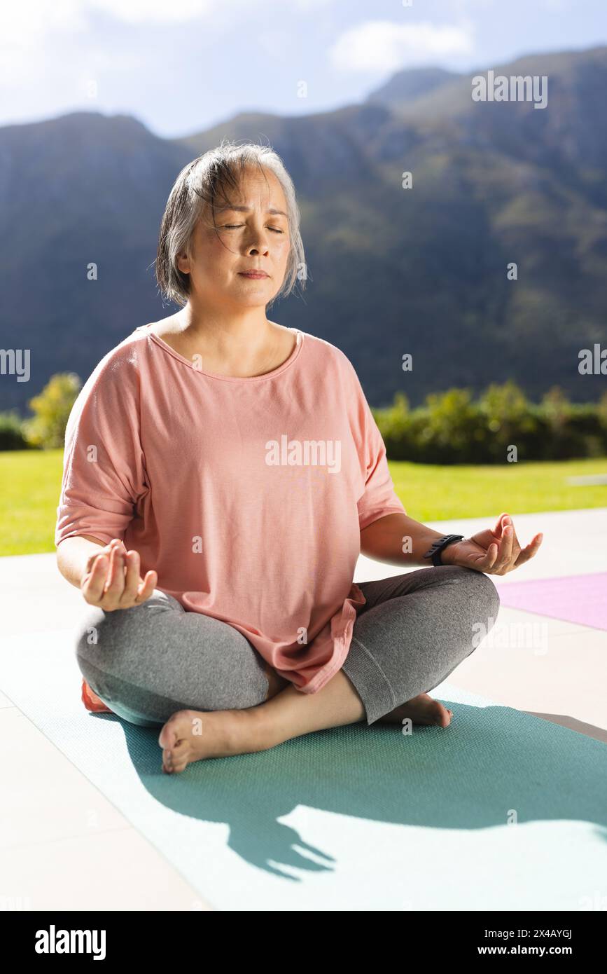Asian senior woman sitting cross-legged on yoga mat, meditating ...