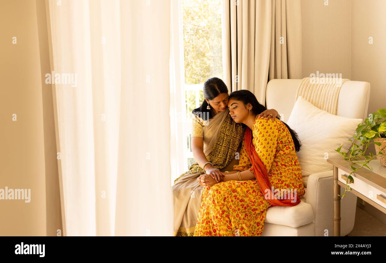 Indian mother comforting teenage daughter on sofa, both in traditional ...