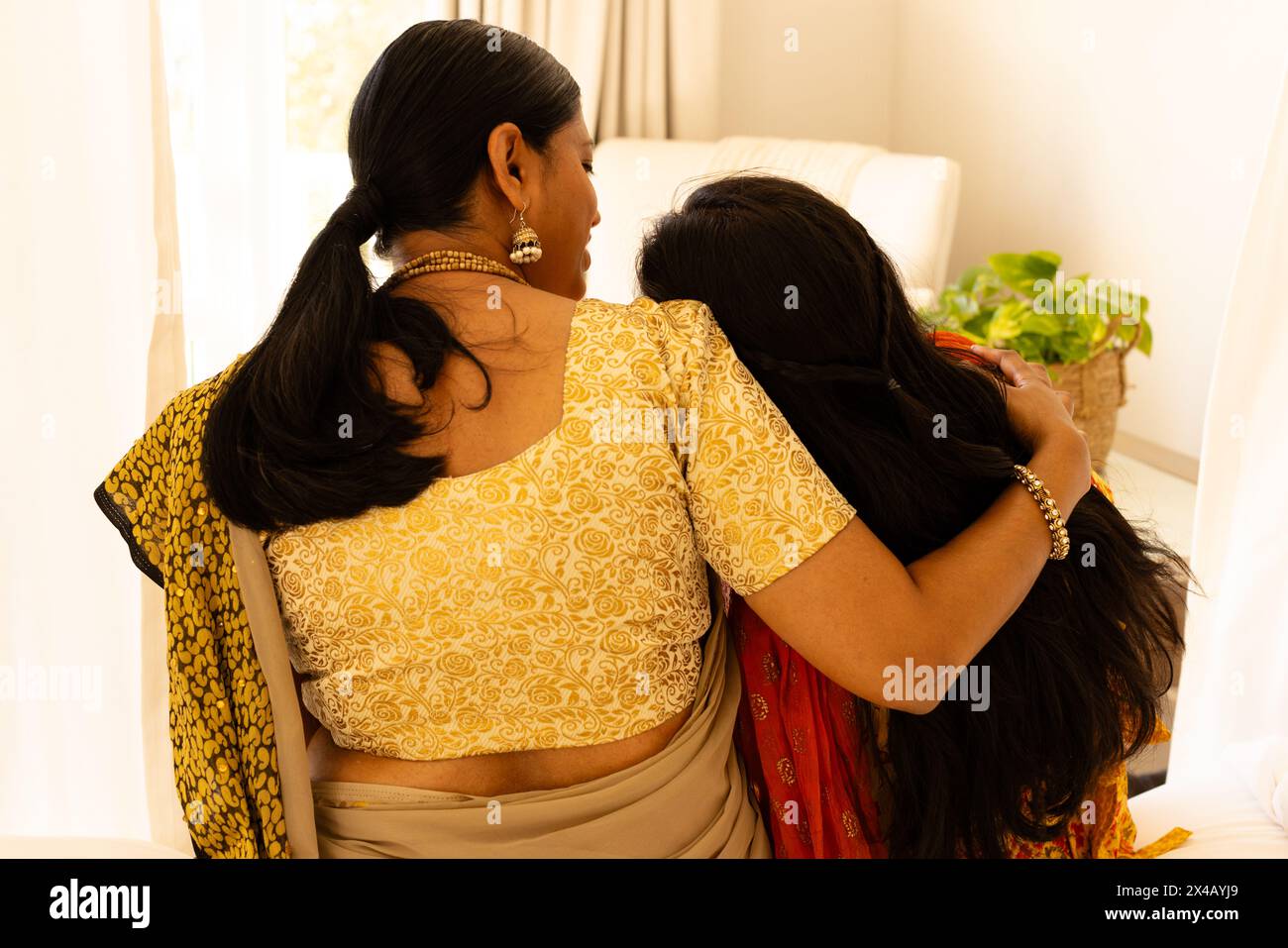 Indian mother and teenage daughter, hugging warmly at home. Both wearing traditional Indian ...