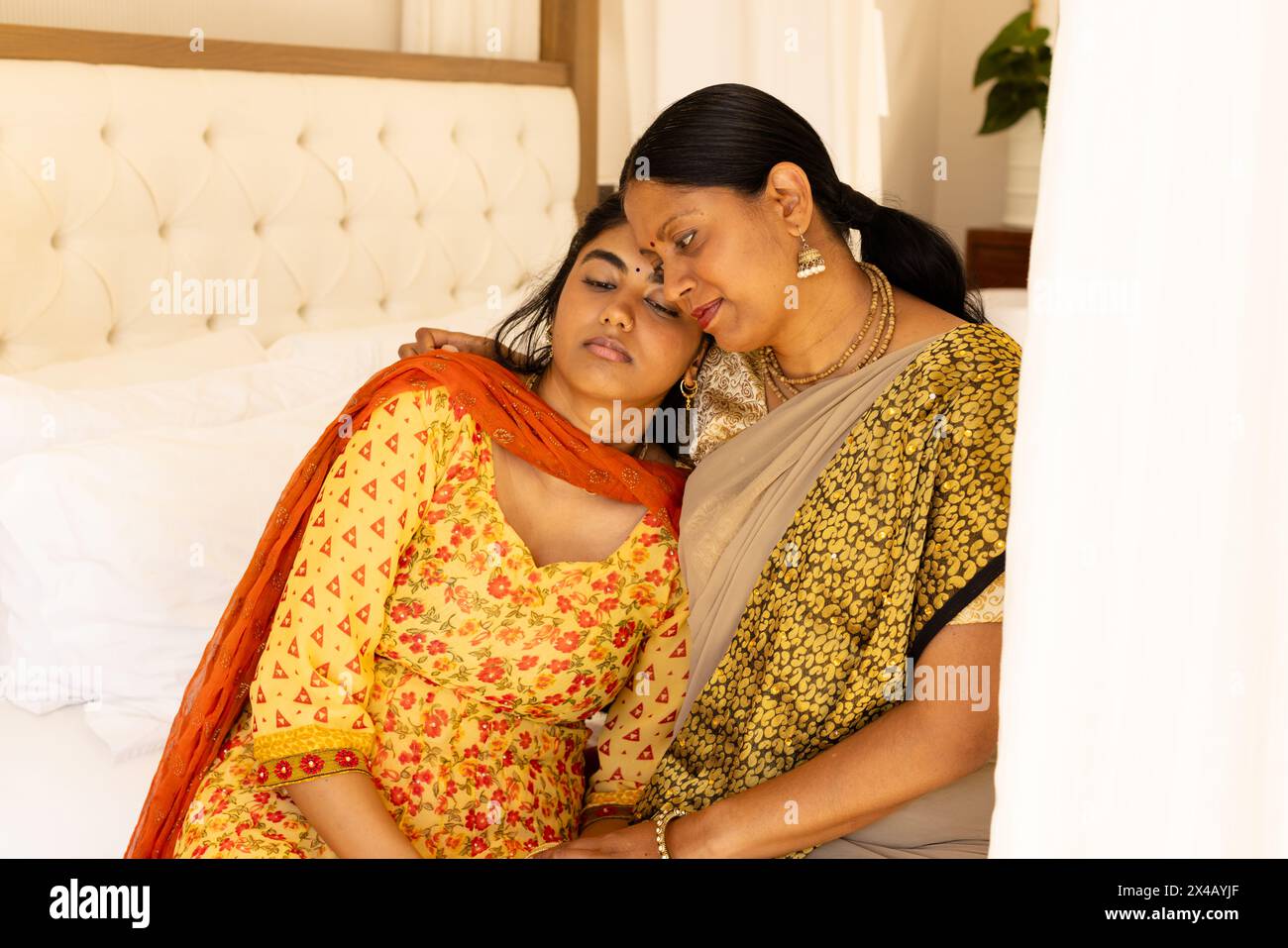 Indian mother and teenage daughter embracing on bed, wearing ...
