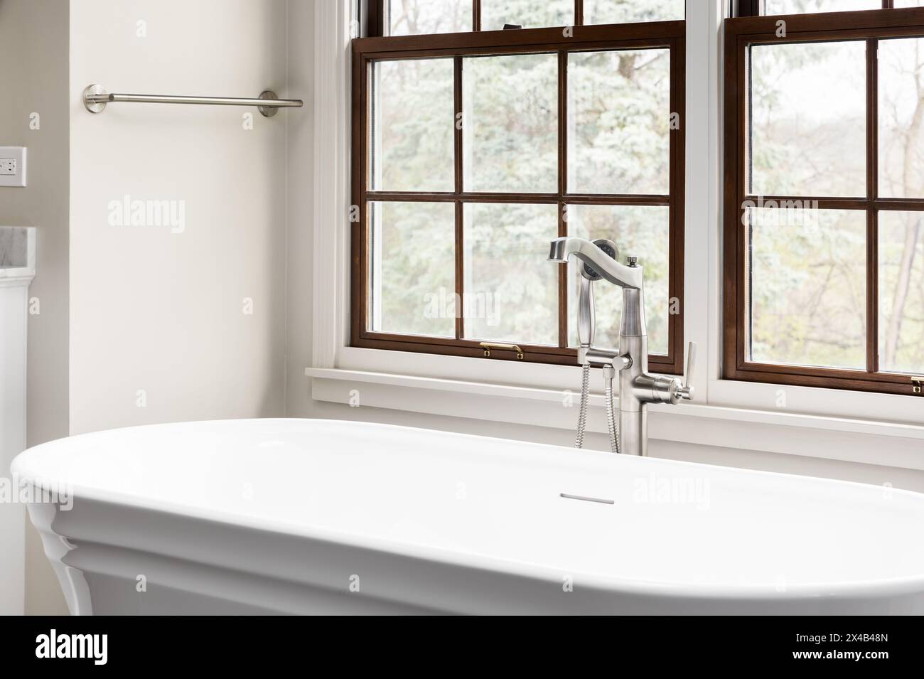 A freestanding bathtub faucet detail in front of a wood framed window ...