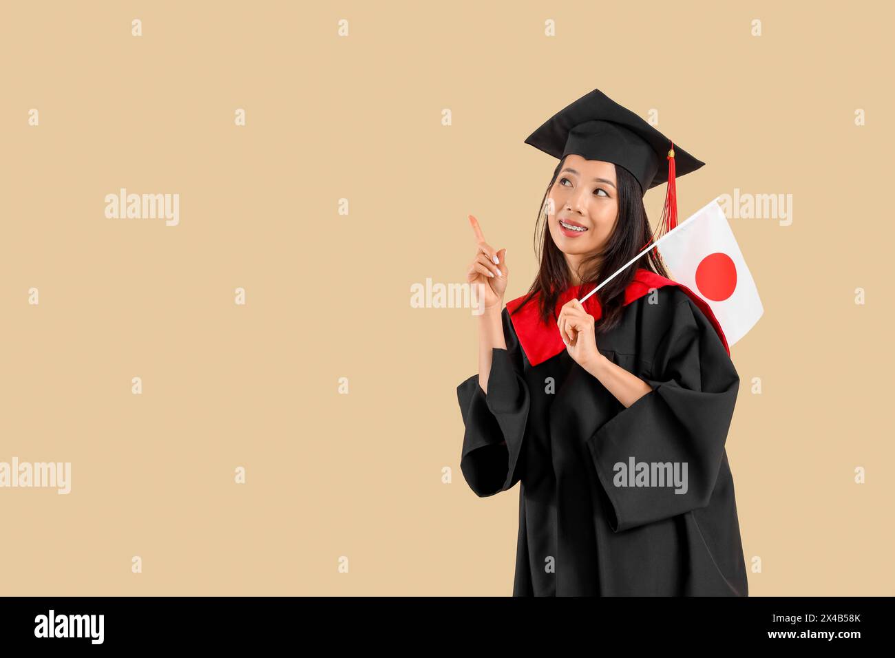Female Asian graduate with flag of Japan pointing at something on beige ...