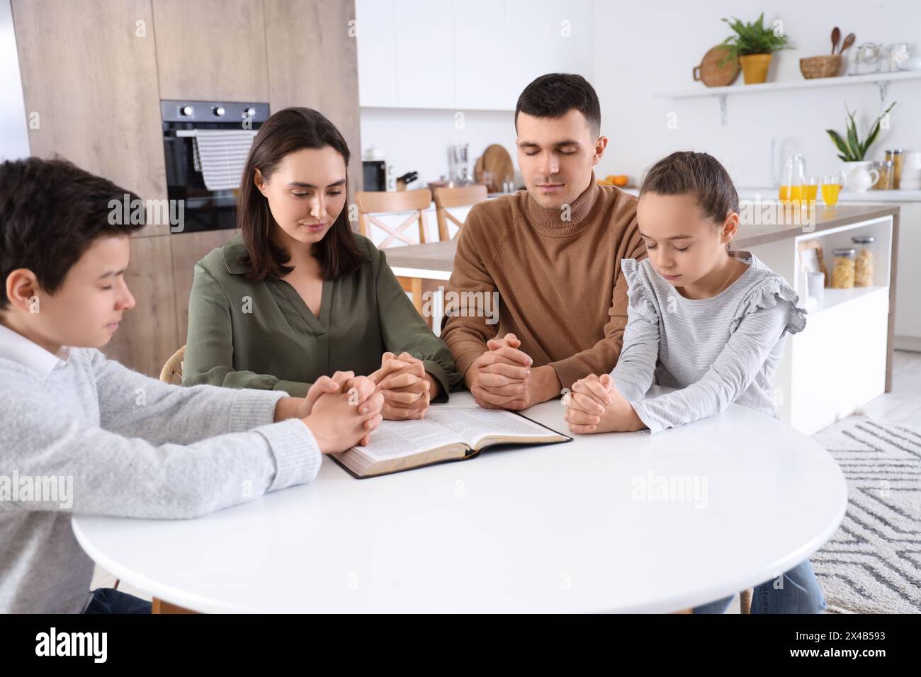 Family praying with Holy Bible on table in kitchen Stock Photo - Alamy