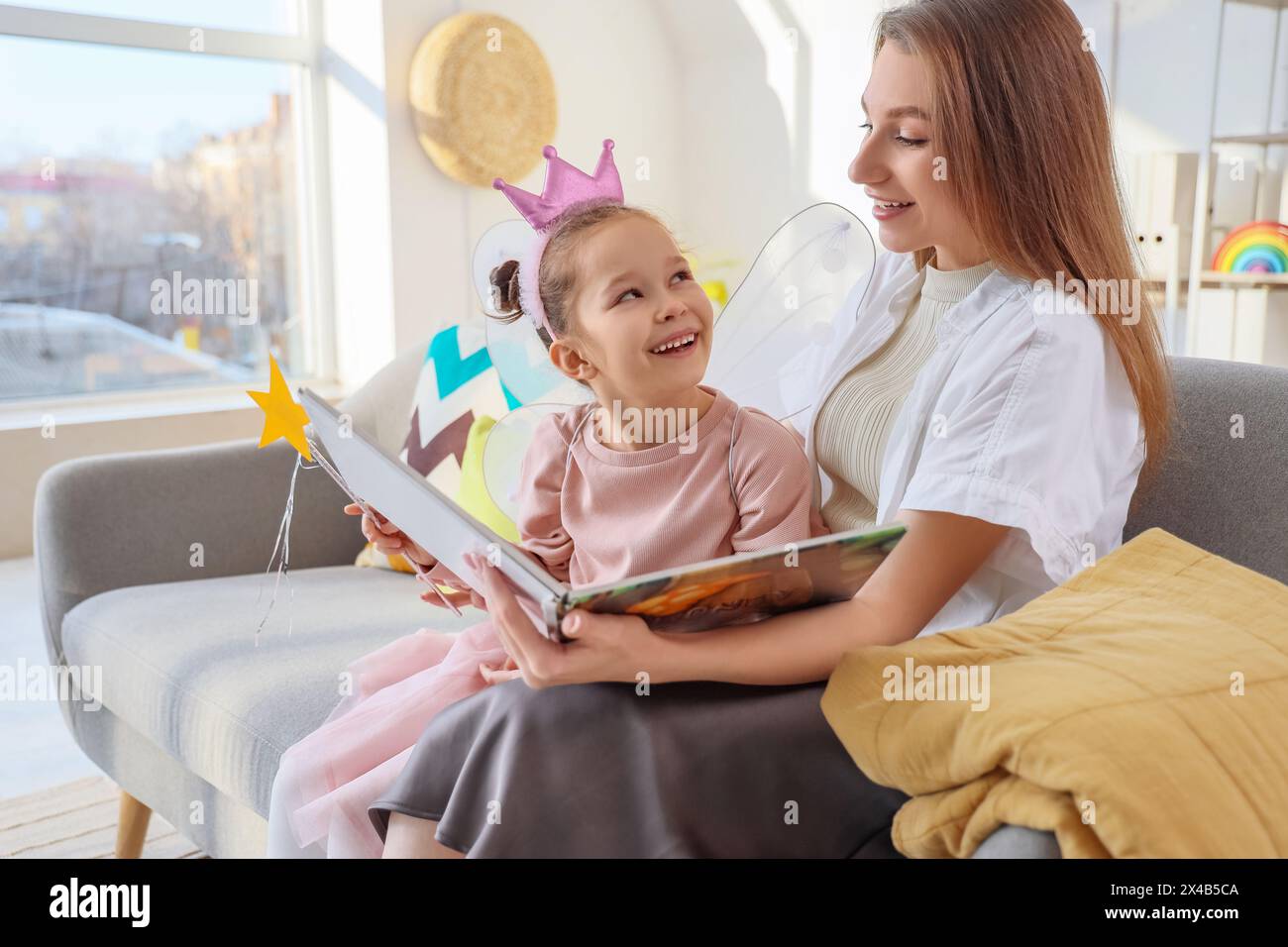 Little girl dressed as fairy with her mother reading story at home ...