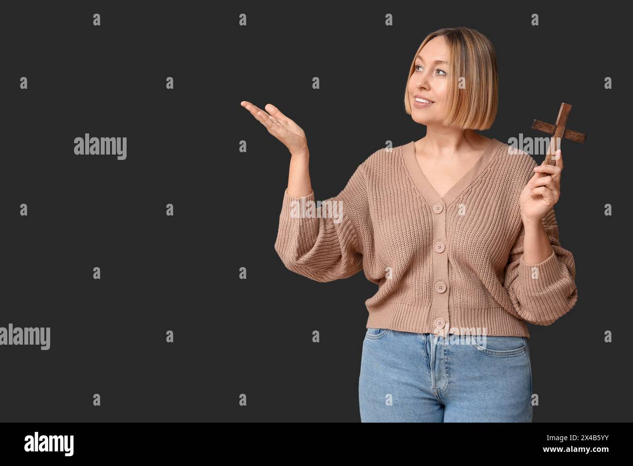 Happy adult woman with wooden cross pointing at something on black ...