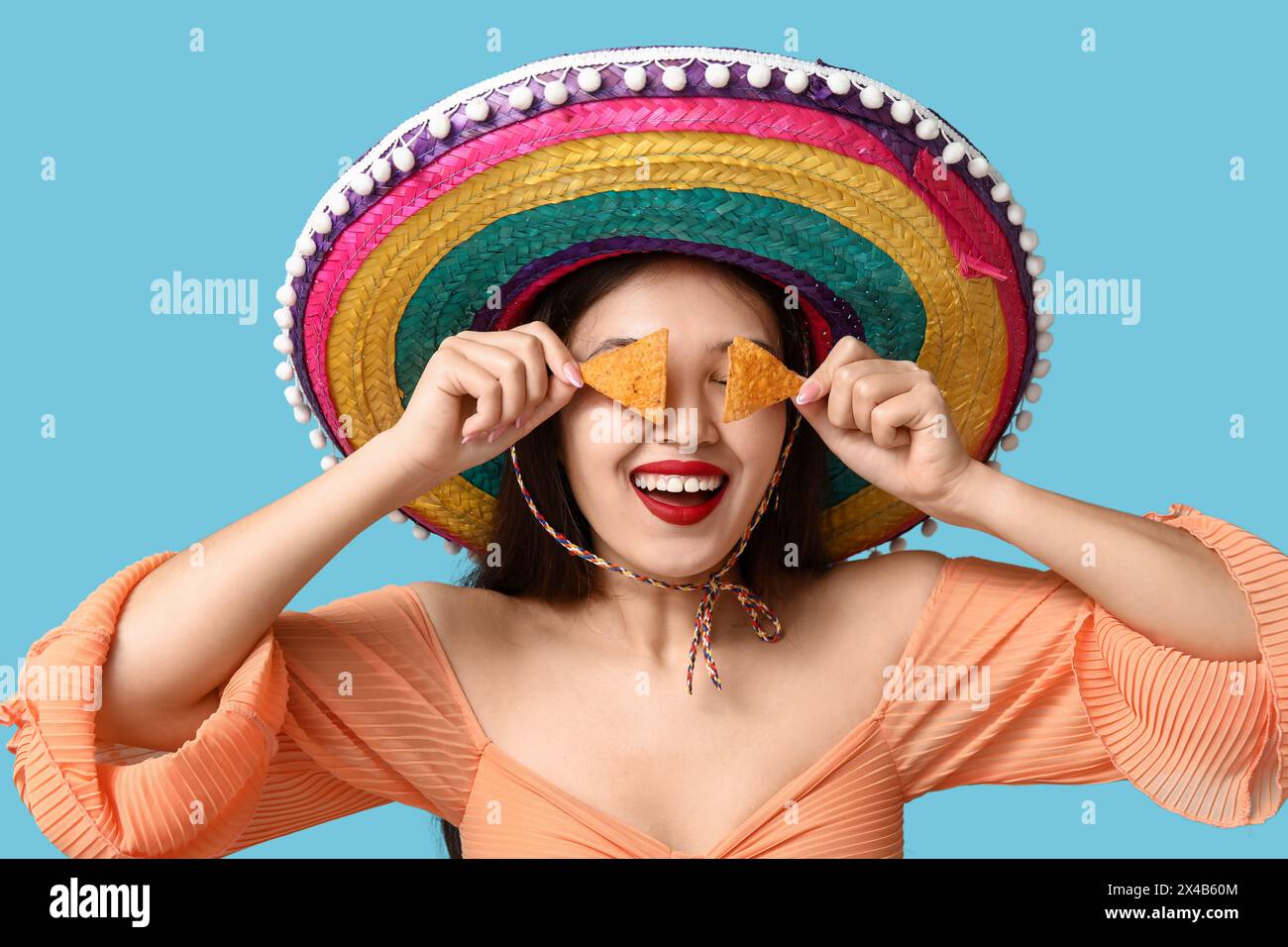Portrait of young woman with sombrero and tortilla chip on blue ...