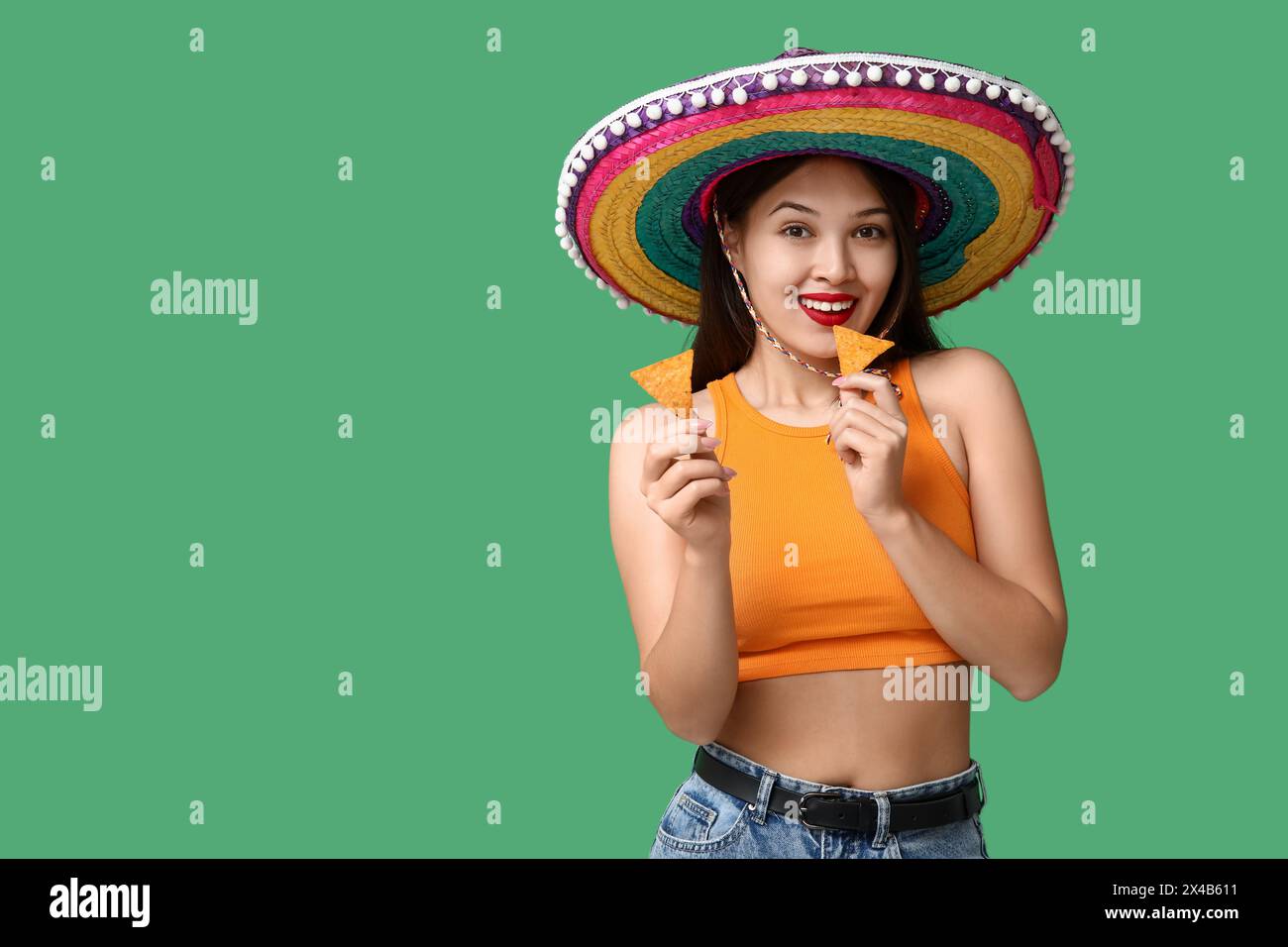 Portrait of young woman with sombrero and tortilla chips on green ...