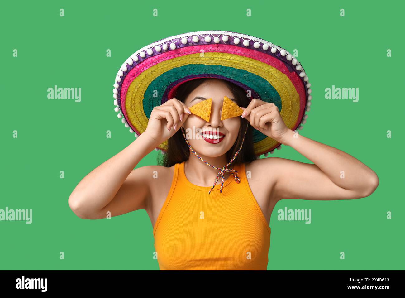 Portrait of young woman with sombrero and tortilla chips on green ...