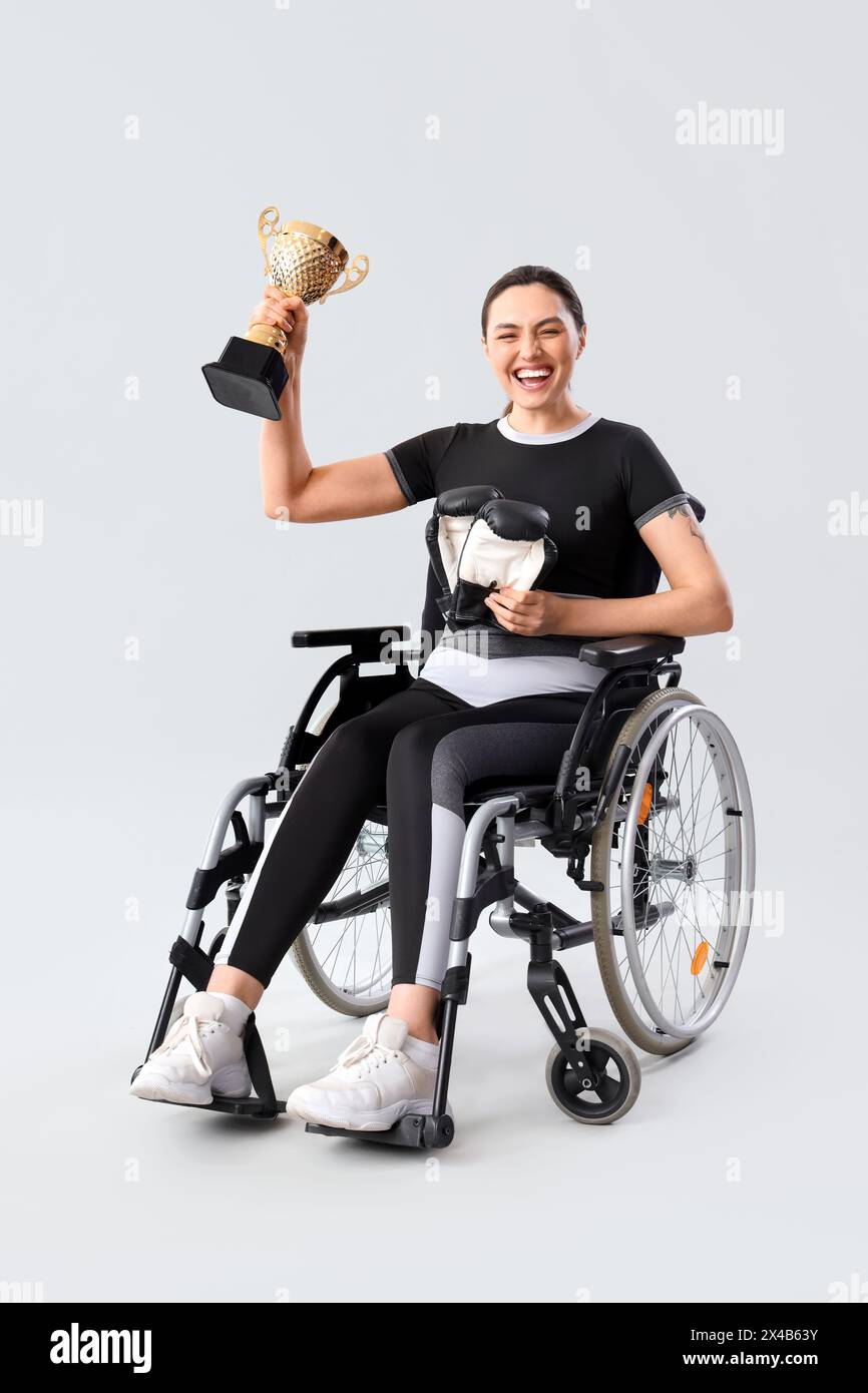 Sporty young woman in wheelchair with boxing gloves and gold cup on ...