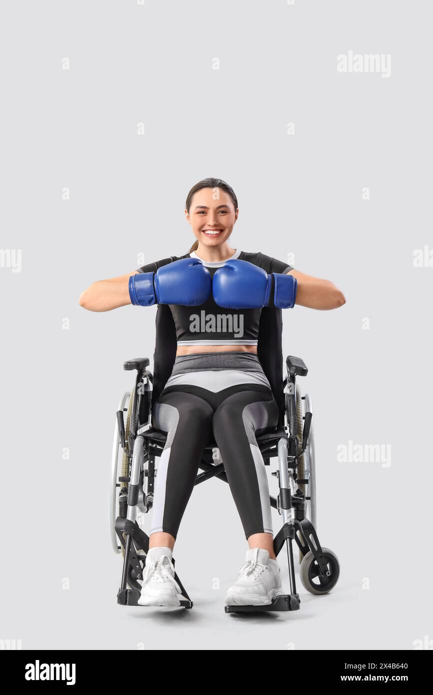 Sporty young woman in wheelchair with boxing gloves on light background ...