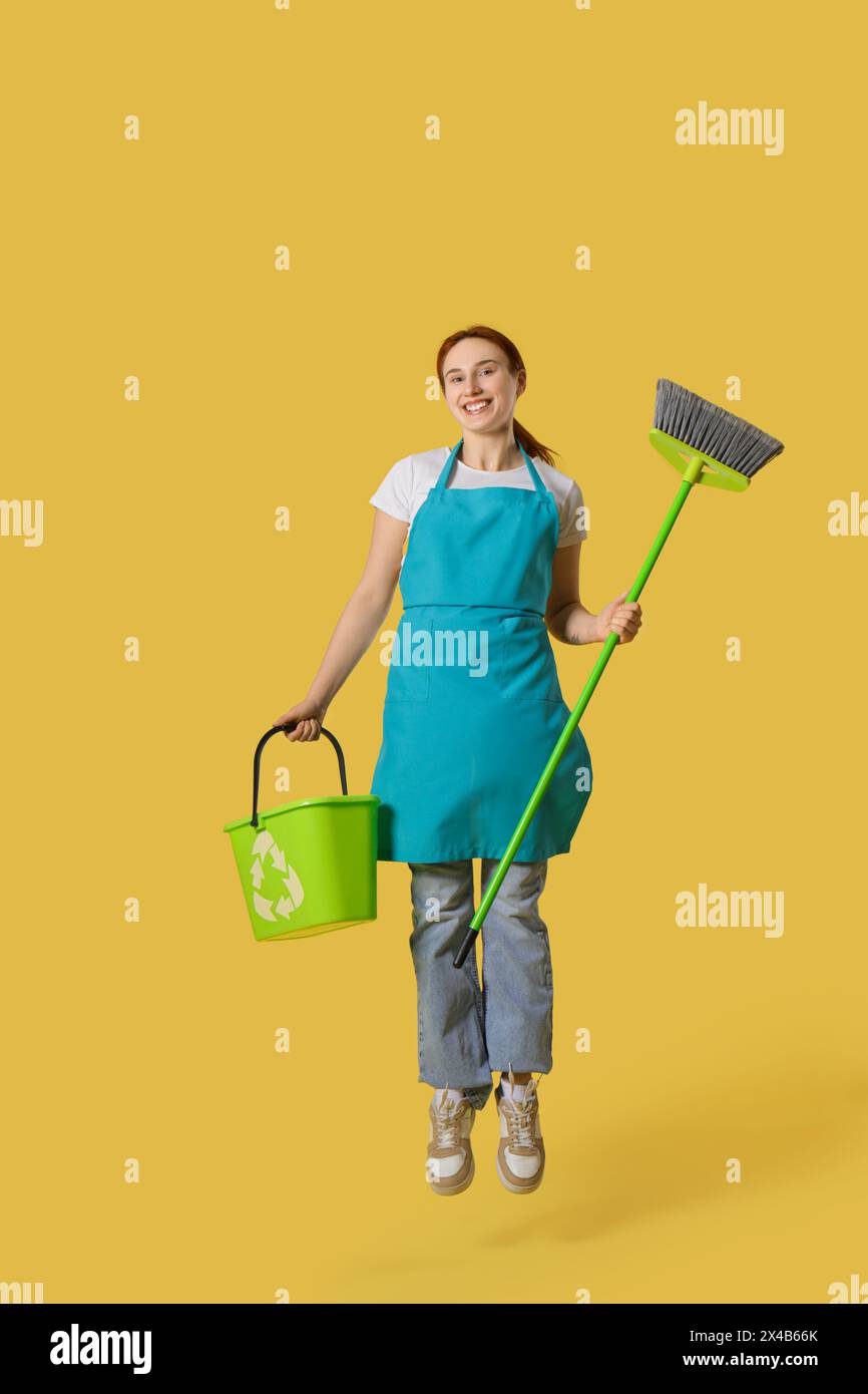 Female janitor with mop and bucket jumping on yellow background Stock ...