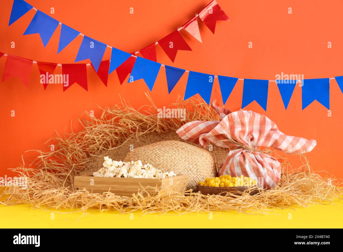 Straw hat, popcorn, corn and flags for Festa Junina celebration on table against color ...