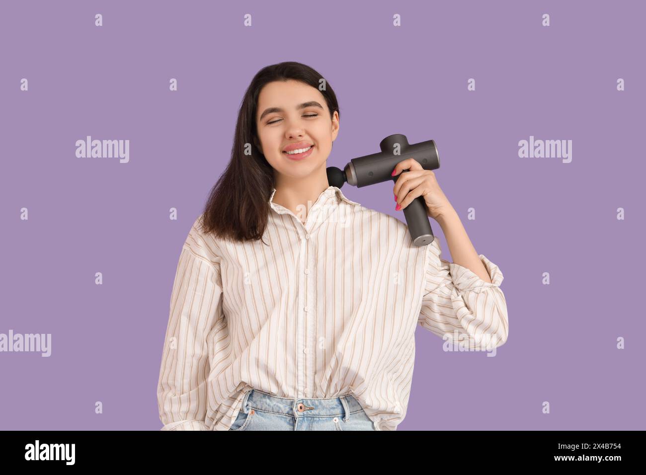 Young woman massaging her neck with percussive massager on lilac ...