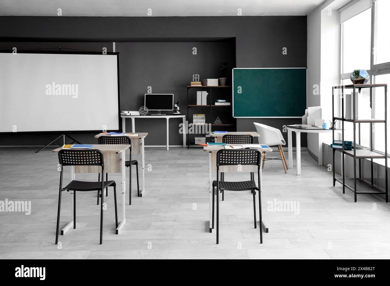 Interior of empty classroom with desks, projector screen and chalkboard ...