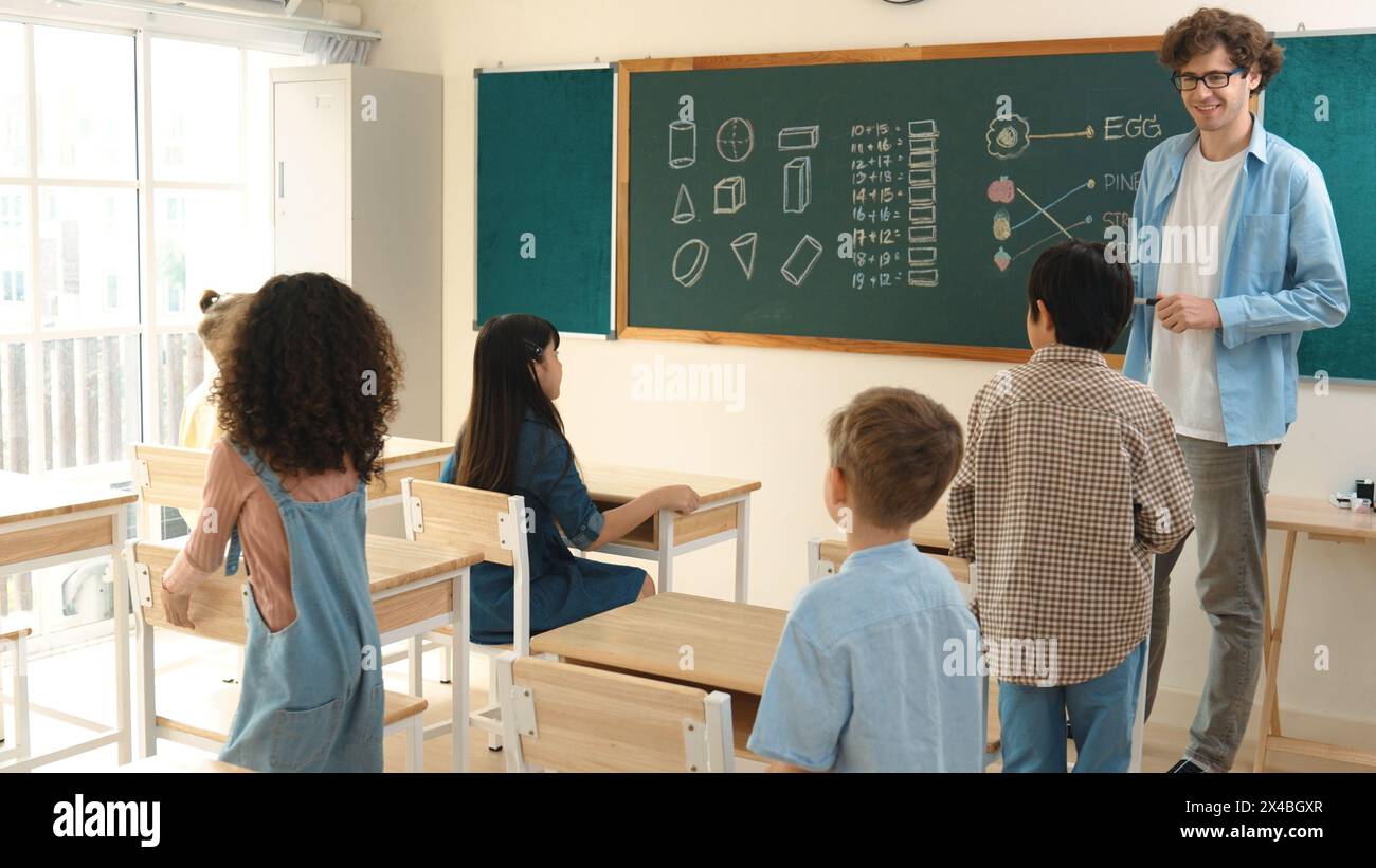 Diverse elementary student walking in classroom while teacher looking ...