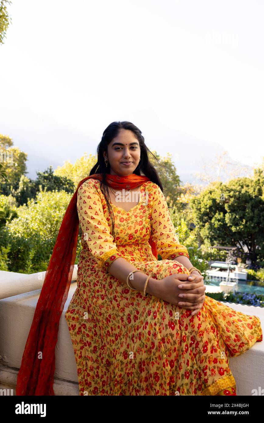 Indian young woman sitting outside, wearing traditional attire. She has ...