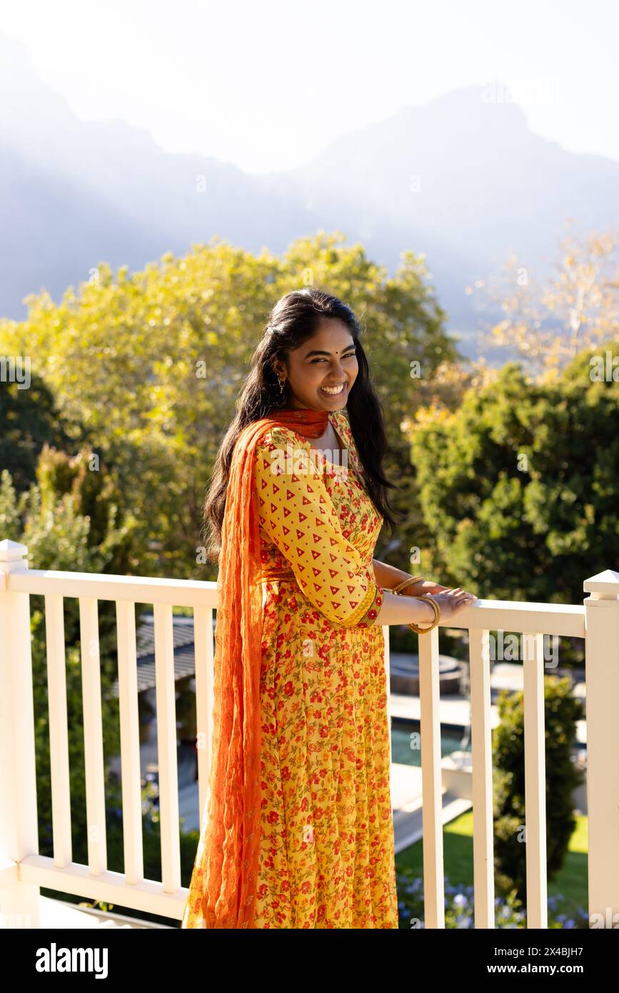 Indian young woman, outdoors, leaning on balcony railing, smiling at ...
